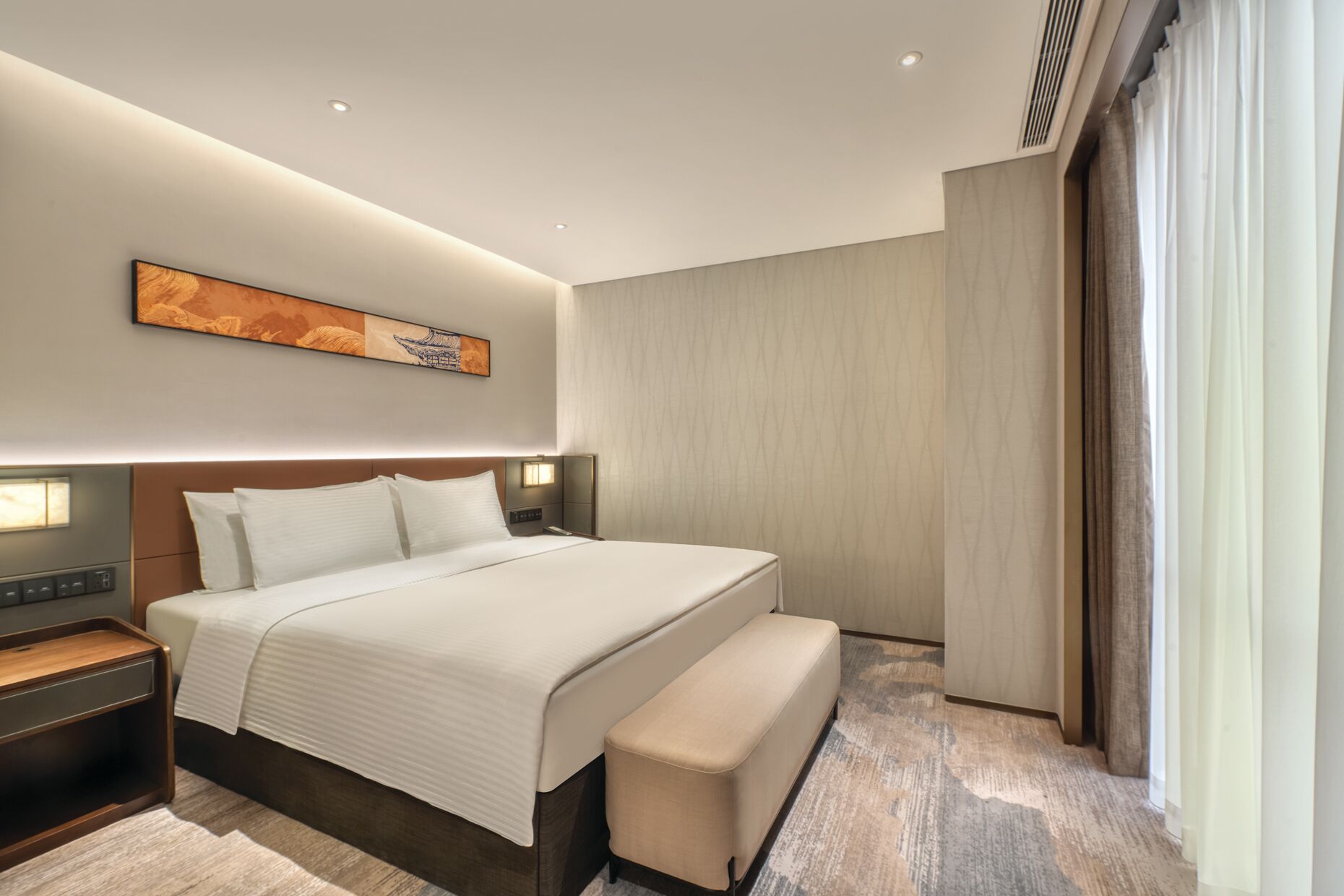 Quarto de hotel moderno com uma cama grande, mesas de cabeceira, um banco, uma obra de arte na parede e uma janela com cortinas.
