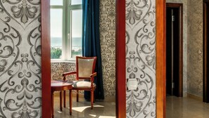 Quarto com um espelho grande, papel de parede estampado, uma cadeira e vista para o exterior pela janela.