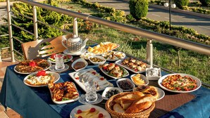 Mesa posta com diversos pratos, um bule e vista para o mar e vegetação.