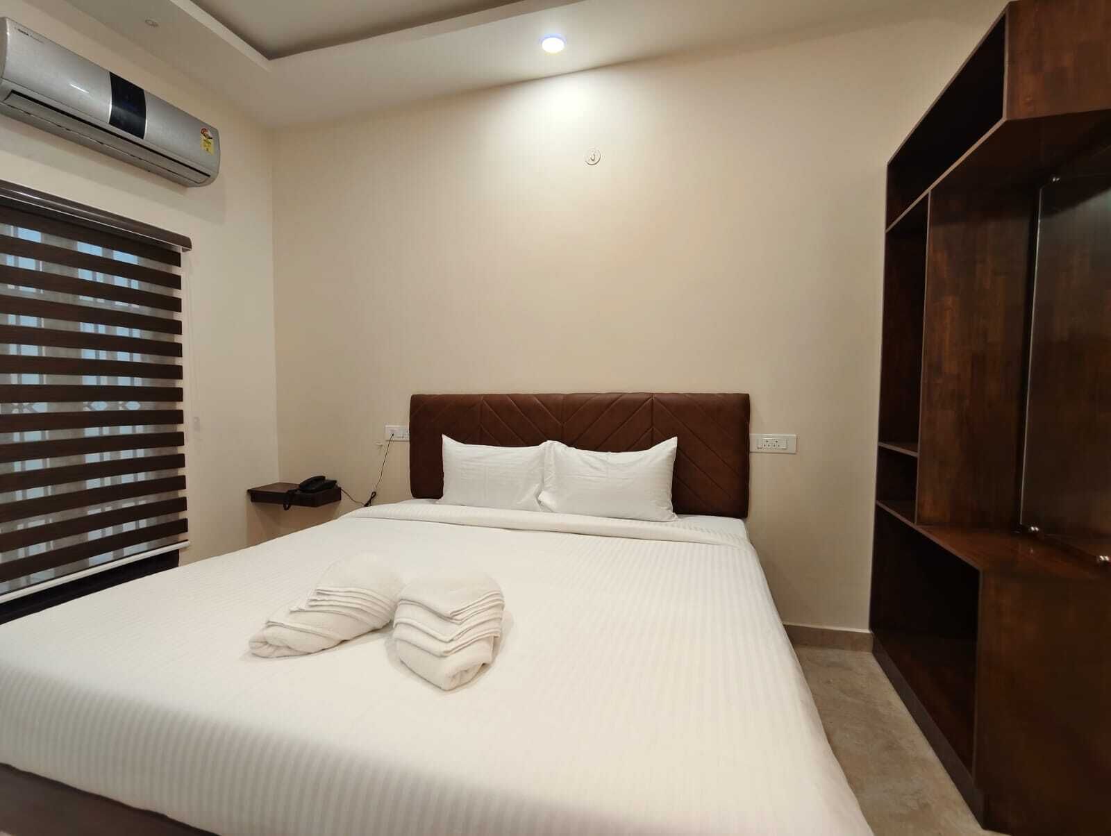 Quarto de hotel com cama, cabeceira de madeira, ar condicionado fixado na parede e guarda-roupa de madeira.