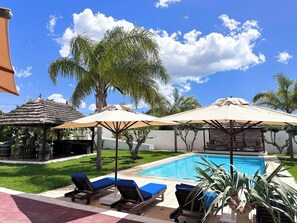 Uma piscina com espreguiçadeiras e guarda-sóis, cercada por palmeiras e um céu claro.