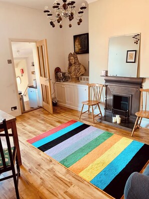 Um quarto com piso de madeira, um tapete listrado e colorido, uma lareira, uma escultura de busto e um candelabro.