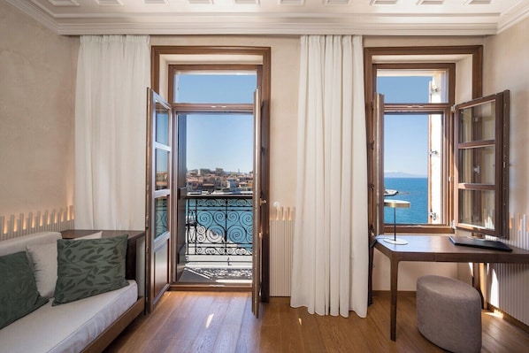 Quarto com varanda, sofá, escrivaninha e vista para o mar.