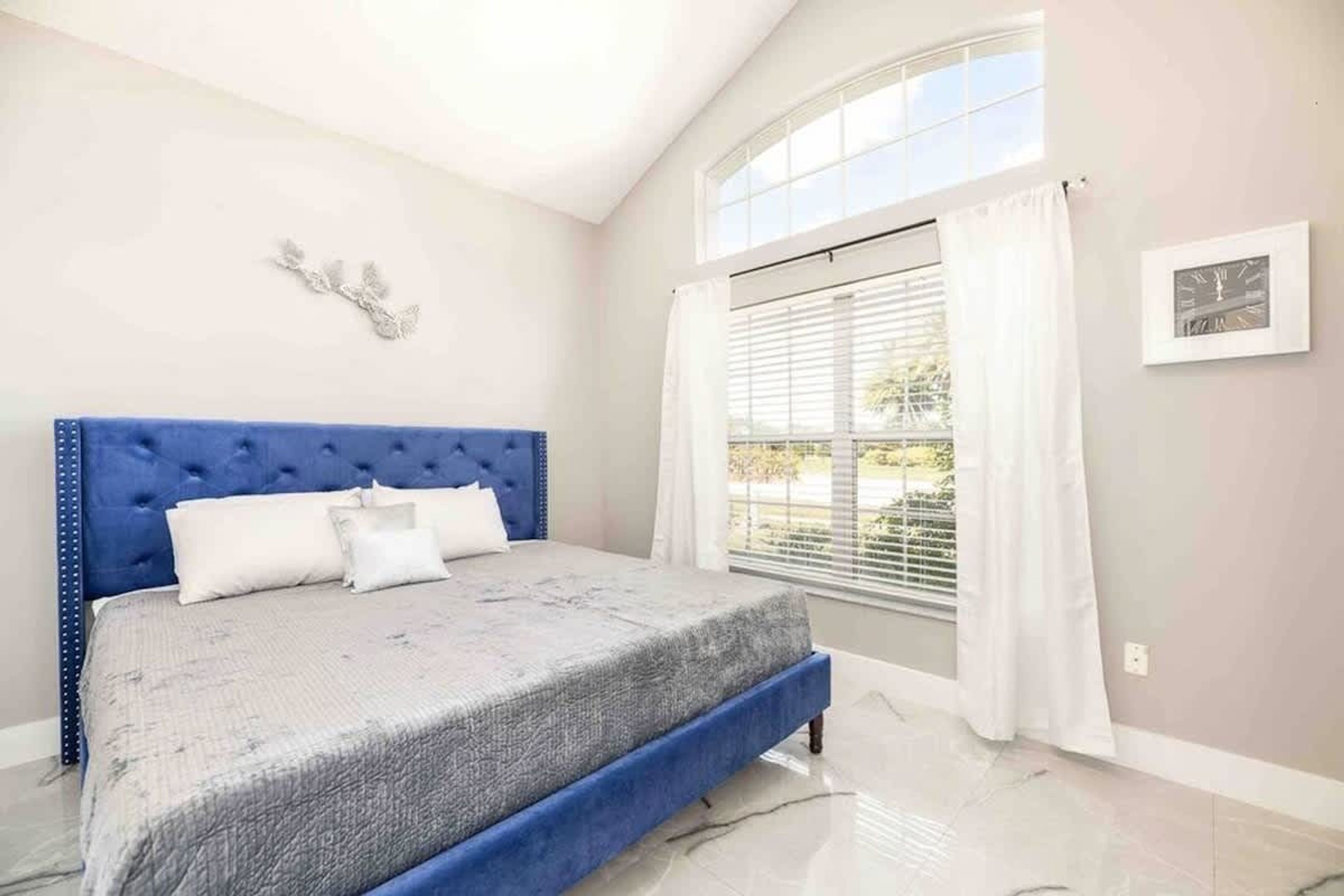 Quarto com uma cama grande, janela com persianas e um relógio na parede.
