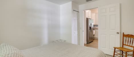 Um quarto com uma cama, uma cadeira e uma porta que dá para uma cozinha.