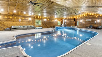 Piscina interna com teto e paredes de madeira, cercada por áreas de estar e um ventilador de teto.