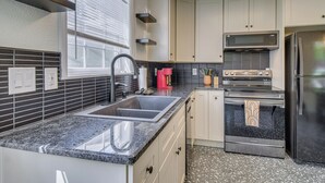 Uma cozinha moderna com bancada de granito, eletrodomésticos de aço inoxidável e painel de azulejos pretos.
