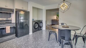 Uma cozinha moderna com eletrodomésticos de aço inoxidável, máquina de lavar e secadora embutidas e um espaço de jantar com mesa redonda e cadeiras.