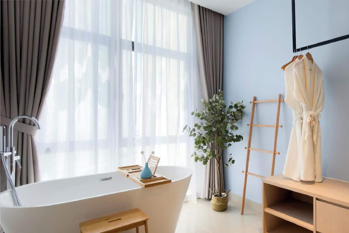 Um banheiro moderno com banheira, toucador de madeira, uma planta e um roupão pendurado em um porta-roupões.