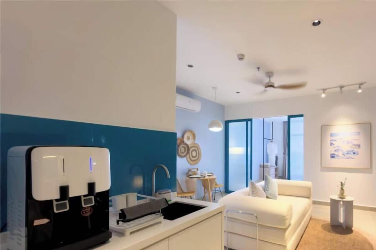Quarto de hotel moderno com cozinha compacta, cama, pequena área de estar e vista pela janela.