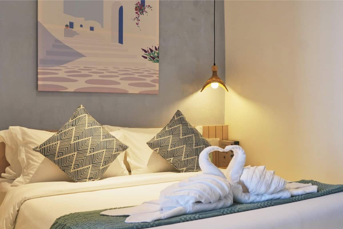 Quarto de hotel com uma cama, almofadas, luminária na parede e um quadro.
