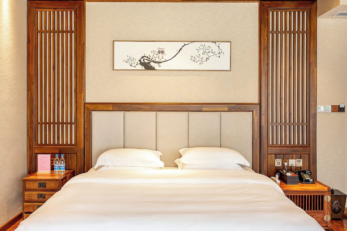 Quarto de hotel com uma cama, mesa de cabeceira com telefone, obra de arte na parede e painel de madeira.