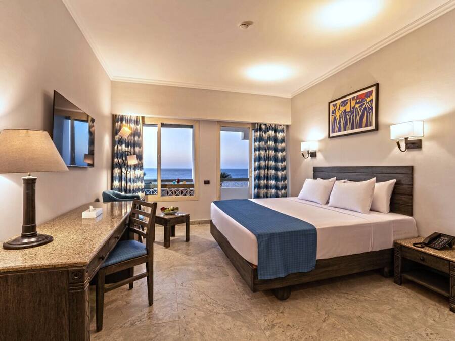 Quarto de hotel com cama, escrivaninha, cadeira e vista para o mar.