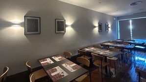 Uma área de refeições com mesas e cadeiras, quadros nas paredes e uma janela grande.