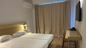Quarto de hotel com duas camas, uma escrivaninha, uma cadeira, uma televisão e uma lixeira.
