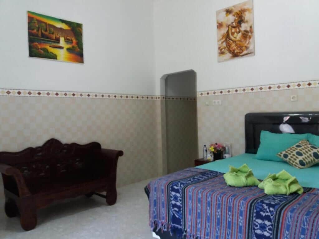 Quarto com uma cama, um banco e duas pinturas na parede.