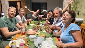 Um grupo de pessoas jantando em uma mesa de madeira, com diversos pratos, uma garrafa e uma lata.