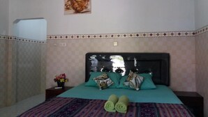 Quarto com cama, almofadas, um quadro na parede e uma mesinha com um vaso de flores.