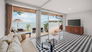 Sala moderna com uma grande porta de vidro que dá para a praia, um sofá, uma mesa de centro e uma TV em um armário de madeira.