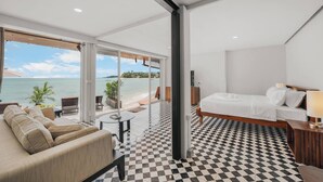 Quarto de hotel com cama, sofá, mesa pequena e vista para o mar.