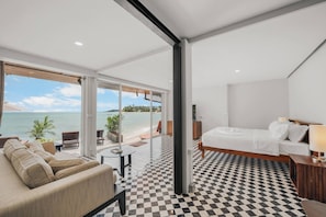 Quarto de hotel com cama, sofá, mesa pequena e vista para o mar.
