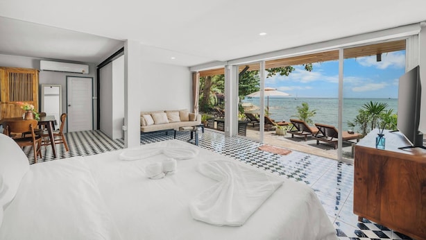 Quarto de hotel com cama, televisão, sofá, mesa de jantar e vista para o mar.