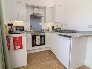 Cozinha compacta com armários brancos, micro-ondas, torradeira, pia e lava-louças.
