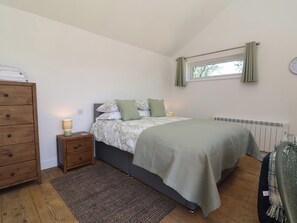 Quarto com cama, mesa de cabeceira, cômoda, janela com cortinas e radiador.