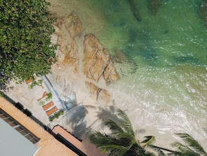 Vista aérea de uma praia com águas claras, costa rochosa e palmeiras.