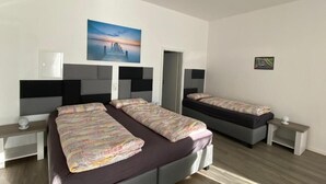 Quarto de hotel com duas camas, uma mesinha de cabeceira, uma escrivaninha, uma cadeira, um quadro e uma porta.