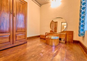 Um guarda-roupa de madeira, um espelho redondo e um banquinho em um quarto com soalho de madeira.