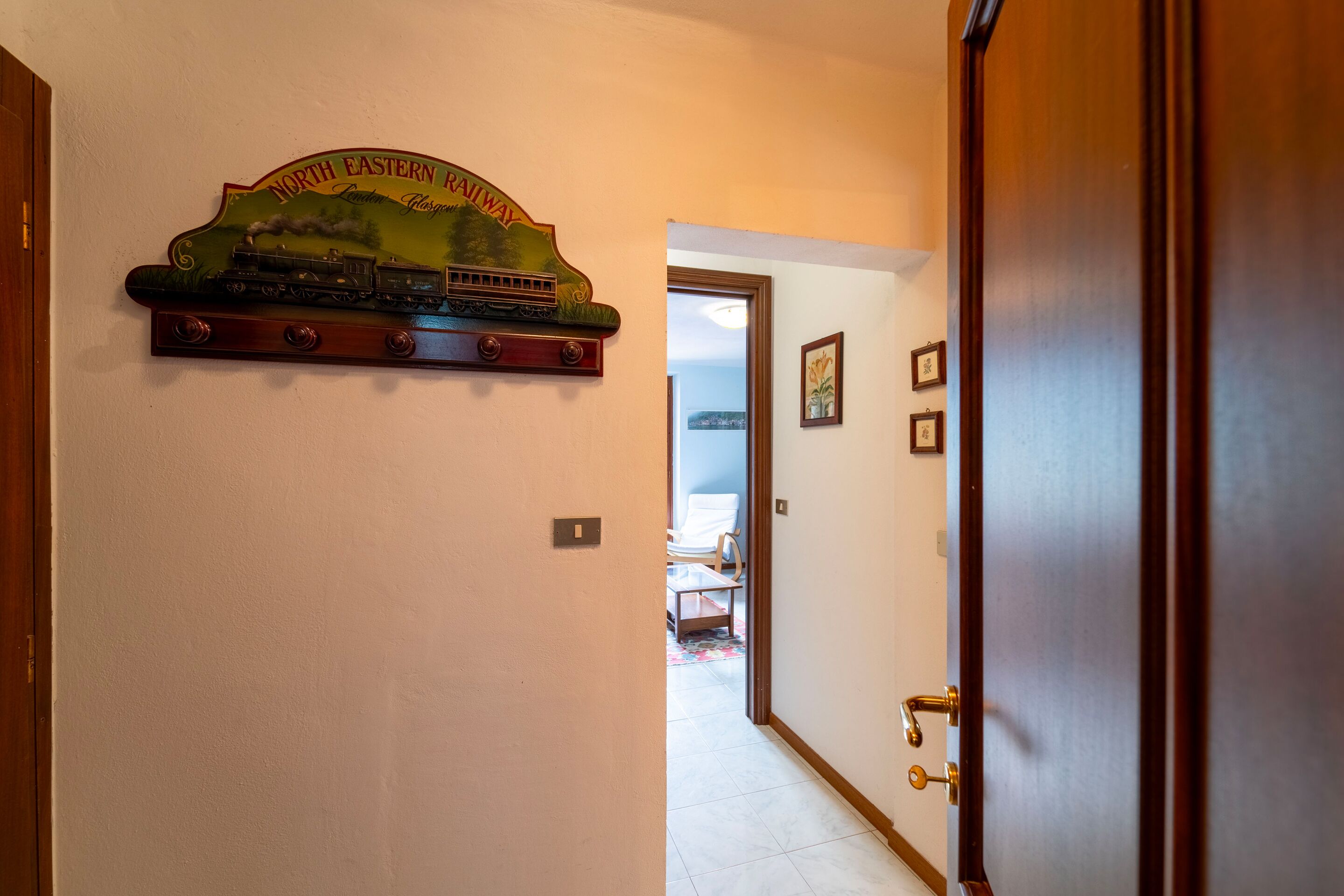 Um corredor com um letreiro da North Eastern Railway, uma porta e um vislumbre de um quarto com uma cadeira e uma mesa.