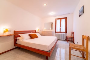 Quarto com cama de madeira, mesa de cabeceira, cadeira, cômoda, espelho e janela com cortinas.