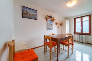 Uma sala de jantar com uma mesa e cadeiras de madeira, um radiador branco e uma janela com vista.