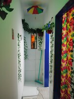 Um corredor estreito com ventoinha no teto, um esfregão e plantas penduradas.