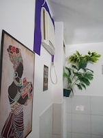 Quarto com uma obra de arte emoldurada, um vaso de planta e uma placa na parede.