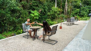 Área externa com mesas e cadeiras, cercada por vegetação densa.