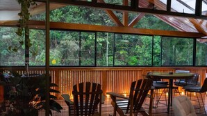 Quarto com grandes janelas, piso de madeira e uma mesa com cadeiras.