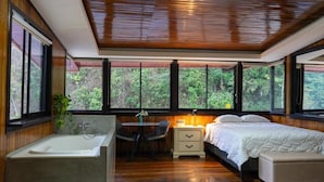 Quarto com uma janela grande, banheira, mesa de cabeceira e cama.
