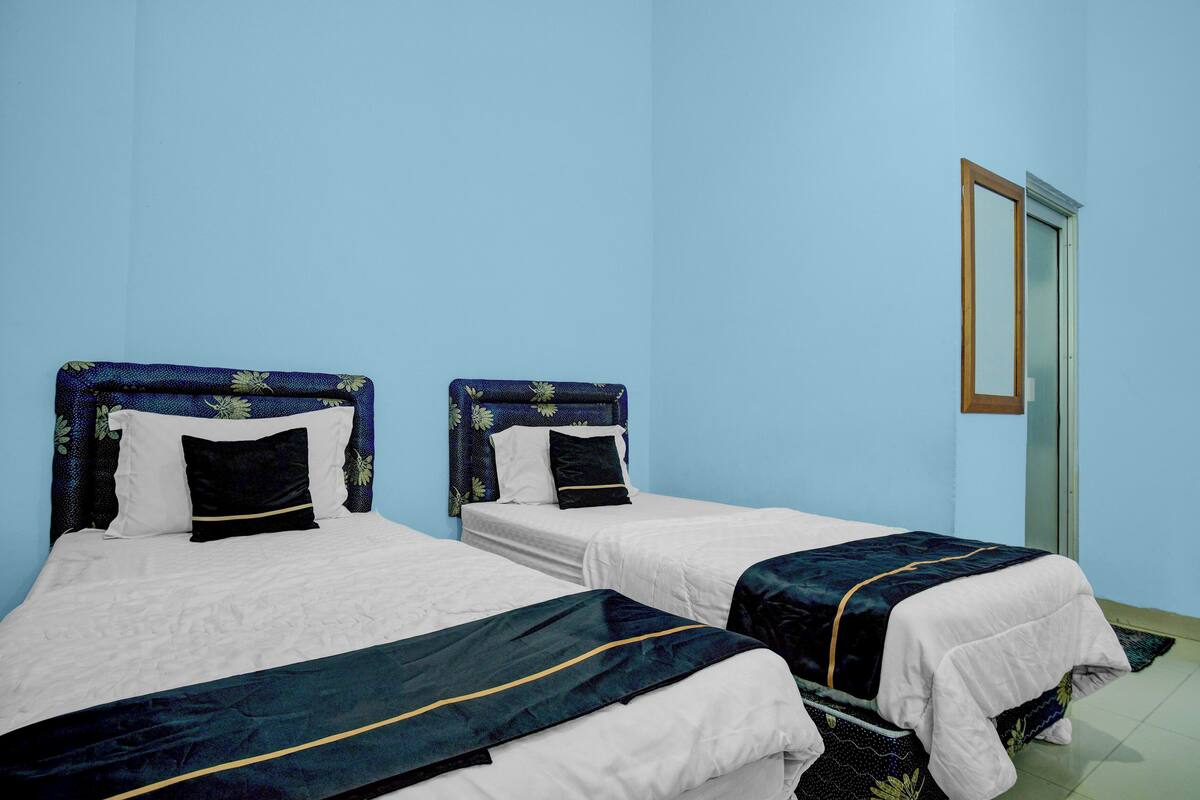 Duas camas de solteiro com cabeceiras, uma parede azul e uma porta.