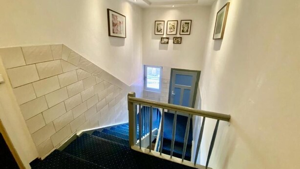 Uma escadaria com corrimão, parede revestida de azulejos e quadros pendurados.