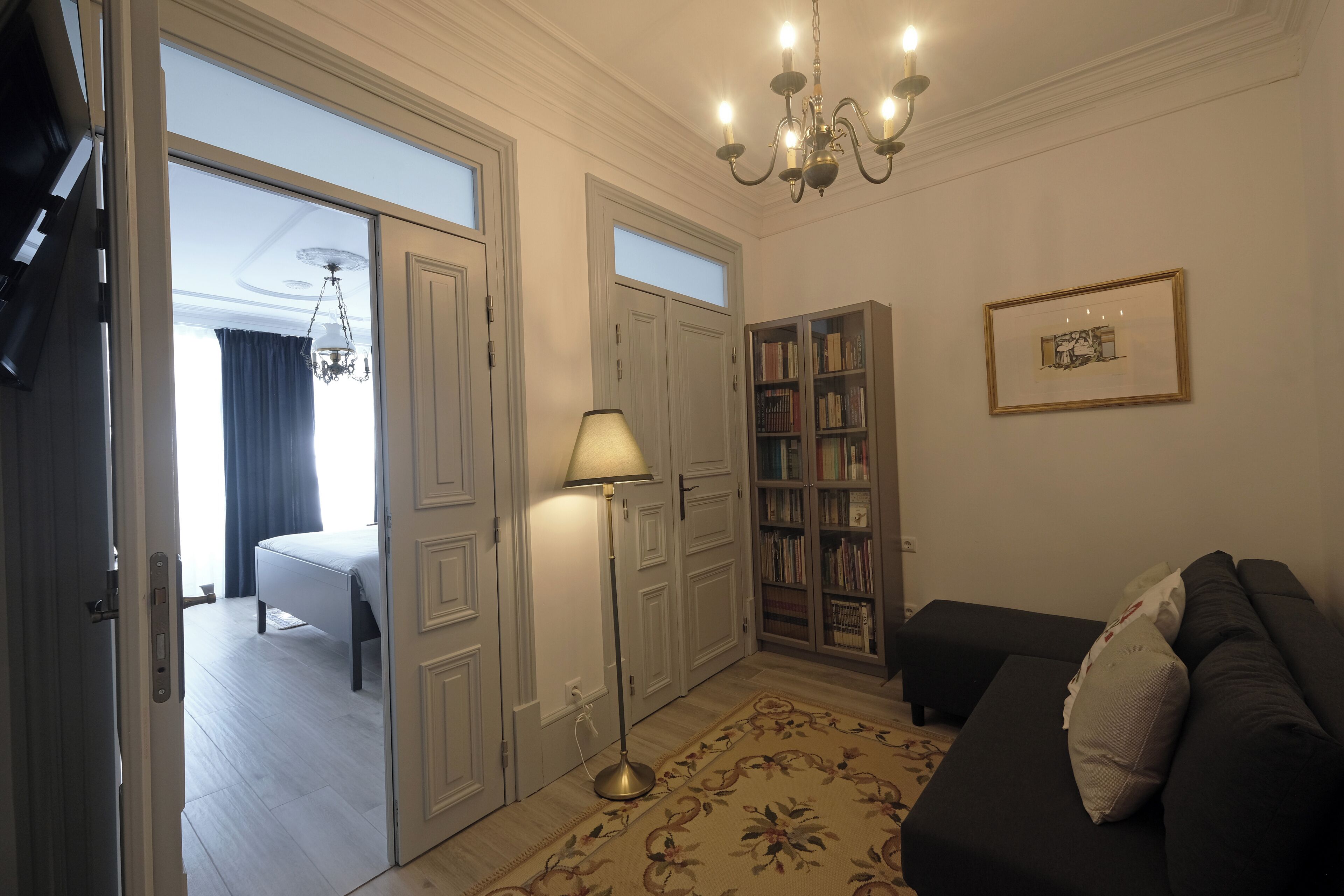 Um quarto com sofá, luminária de chão, estante e porta que dá para outro cômodo.