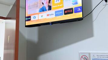 Televisão fixada na parede exibindo diversos serviços de streaming e a indicação da temperatura.