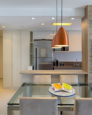 Uma cozinha moderna com uma mesa de jantar de vidro, eletrodomésticos de aço inoxidável e uma luminária pendente.