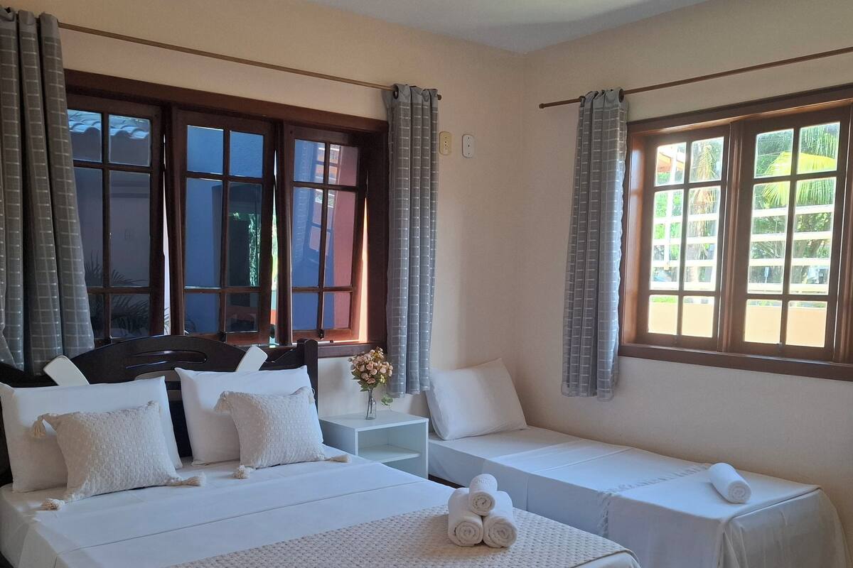 Quarto de hotel com duas camas, uma mesa de cabeceira e uma janela com cortinas.