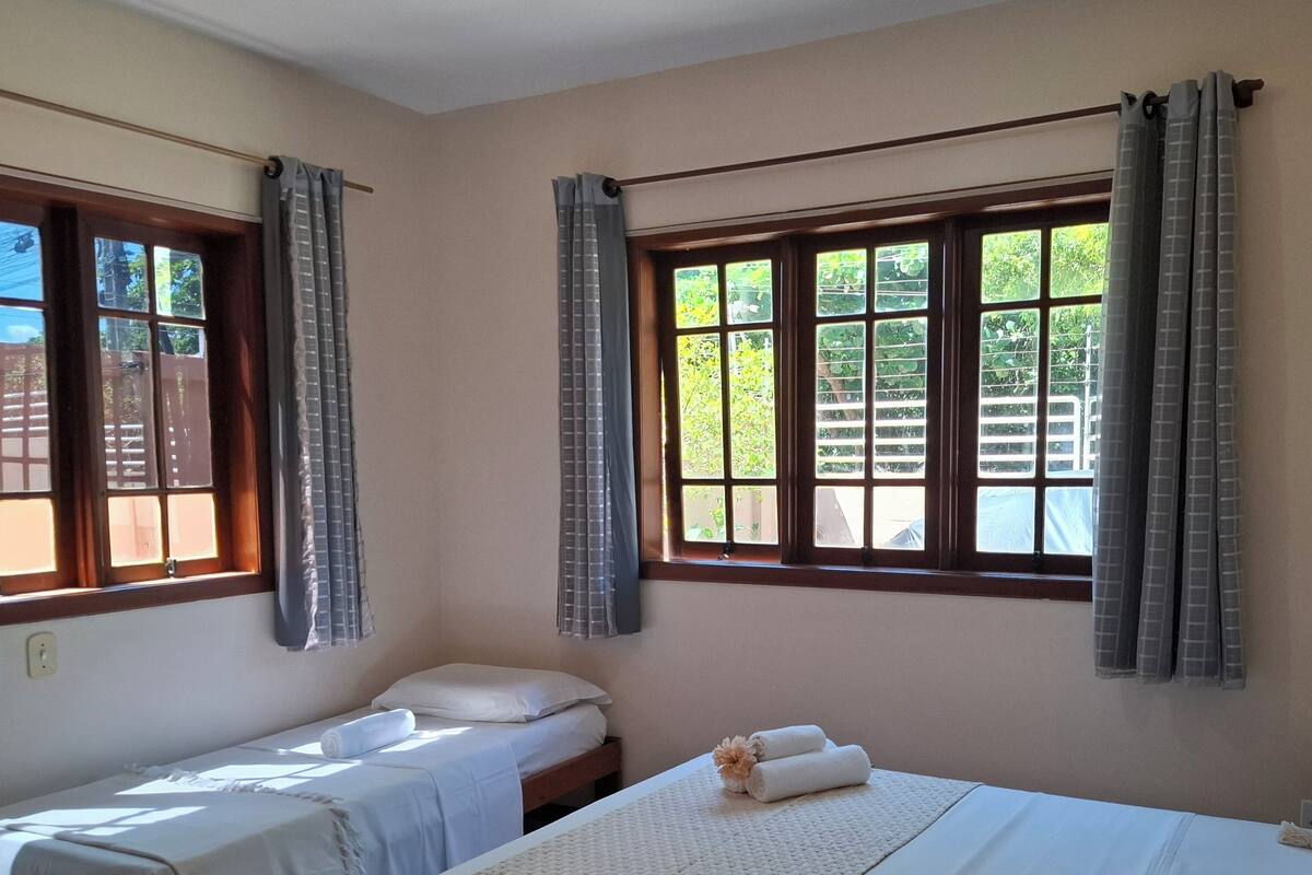 Quarto com duas camas de solteiro, uma cama maior e janelas com cortinas.