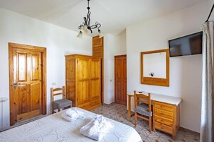 Quarto com cama, guarda-roupa de madeira, escrivaninha, cadeira e televisão na parede.