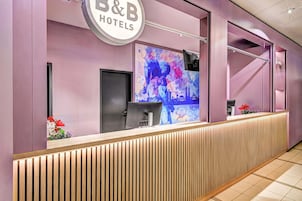 Uma receção com o letreiro 'B&B Hotels', um ecrã digital e painel de design em madeira.