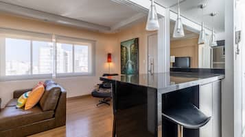 Uma cozinha moderna com bancada preta, área de jantar com sofá de couro marrom e vista para a cidade através de grandes janelas.