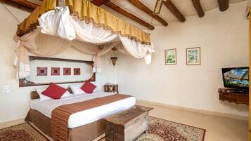 Quarto com cama, um baú de madeira, televisão e ventilador de teto.